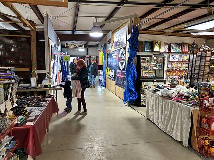 Spacious indoor flea market aisle with vendor booths, snacks, and shoppers browsing the diverse merchandise.