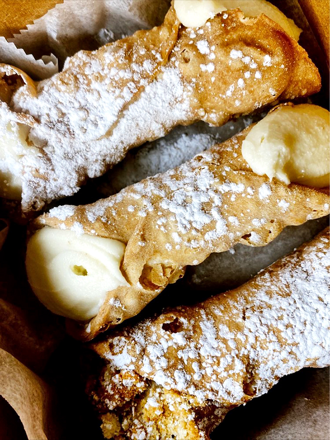 Powdered sugar dusts these golden-brown cannoli shells like fresh snow, with banana cream filling peeking out like a sweet surprise.
