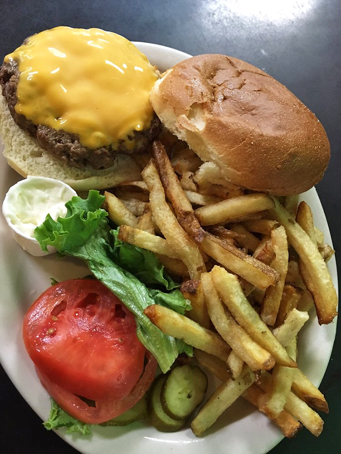 The classic cheeseburger arrives with crispy golden fries and fresh fixings—proof that sometimes the simplest pleasures are the most satisfying.
