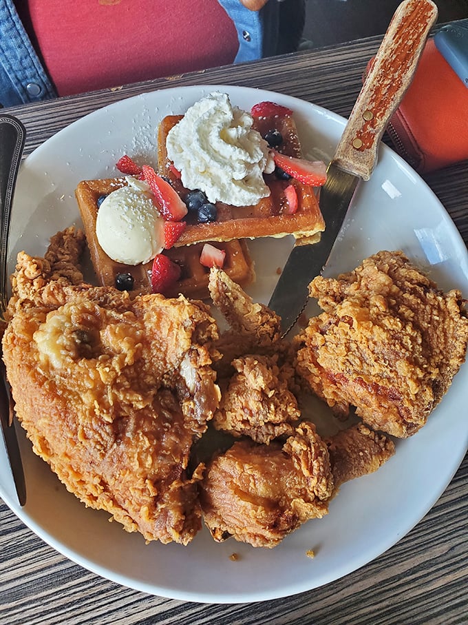 Behold the star attraction: golden-brown fried chicken alongside a Belgian waffle adorned with berries. Crispy, juicy perfection that's worth every calorie.
