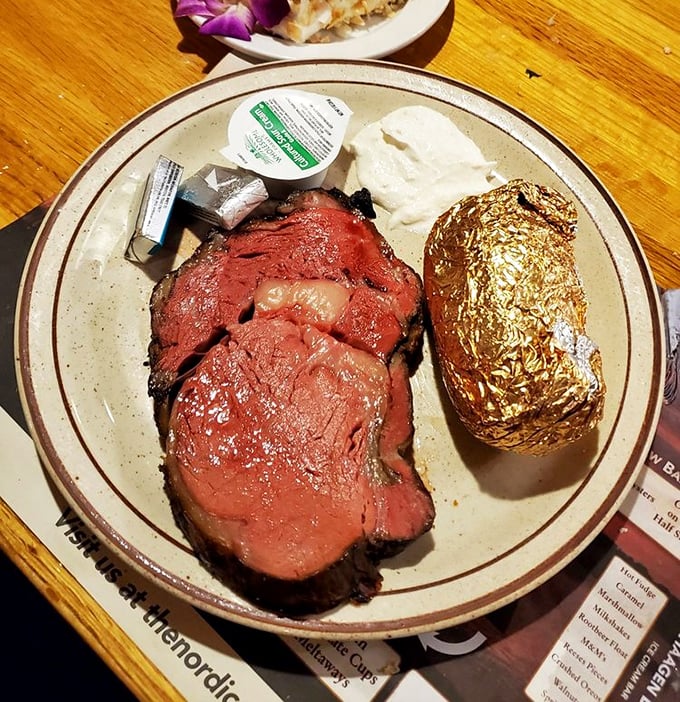 This isn't just prime rib &ndash; it's a carnivore's dream that's been slow-roasted to the exact moment between "heavenly" and "should be illegal." The foil-wrapped potato stands guard.