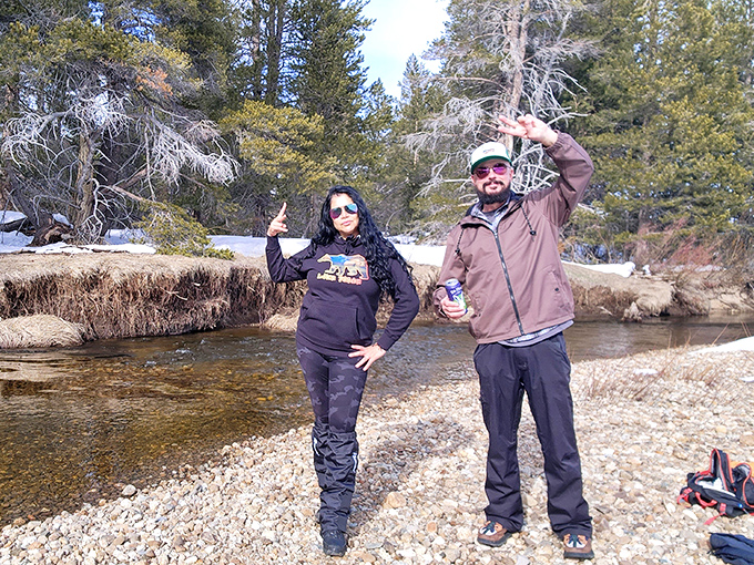Happy explorers toasting to the simple joy of finding a perfect riverside spot where cell phones become irrelevant and conversation flows like the stream.