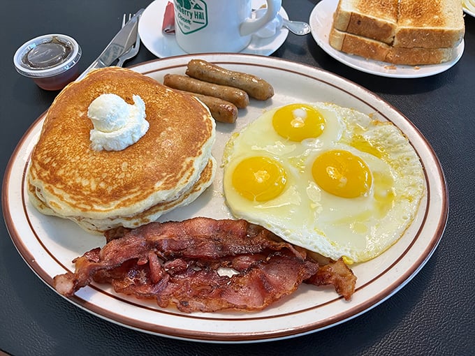 Breakfast perfection on a plate – golden pancakes, sunny-side-up eggs, and bacon that's achieved that magical balance between crispy and chewy.