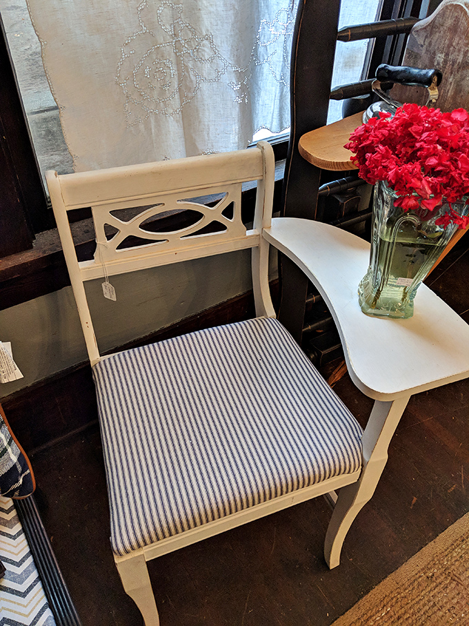 A cream-colored chair with blue striped cushion sits beside vibrant red flowers &ndash; proof that vintage furniture isn't just functional, it's a conversation starter.