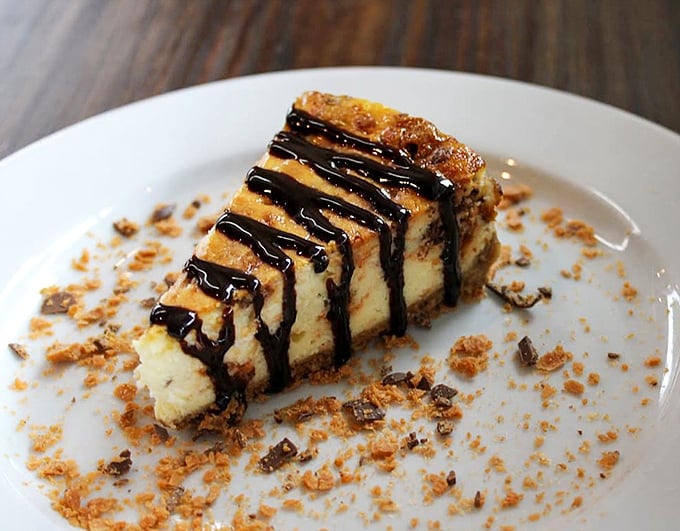This isn't just cheesecake; it's an architectural marvel of creamy decadence, chocolate drizzle, and crumbled crust that makes diets disappear faster than magic.