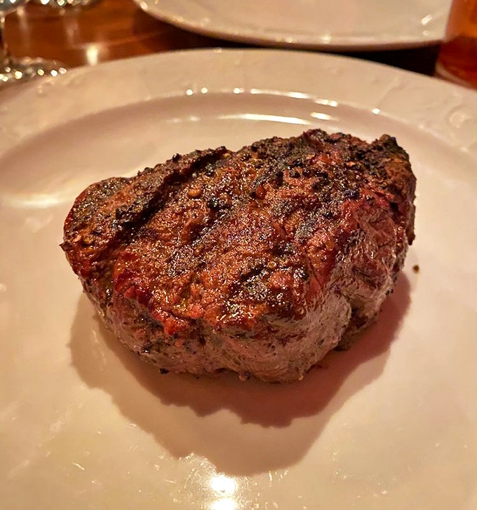 The filet mignon sits regally on its white throne, displaying a textbook sear that gives way to a center so tender it practically dissolves on contact.