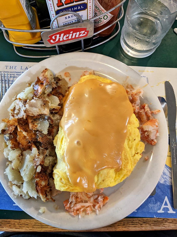 This omelet doesn't just sit on the plate&mdash;it lounges, draped in cheese sauce like it's wearing a velvet robe, with home fries playing the perfect supporting role.