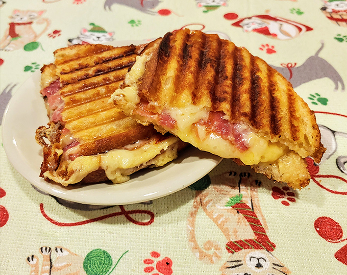 This golden-grilled patty melt oozes with melted cheese on a festive cat-patterned tablecloth – comfort food with feline flair.