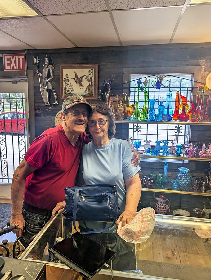 The image shows visitors browsing a colorful display of glassware, with shelves showcasing a rainbow of vintage pieces catching the light.