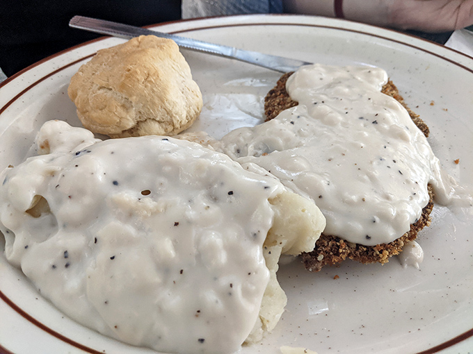 Chicken fried steak smothered in country gravy with a biscuit standing guard. This plate doesn't just feed you—it hugs you from the inside.