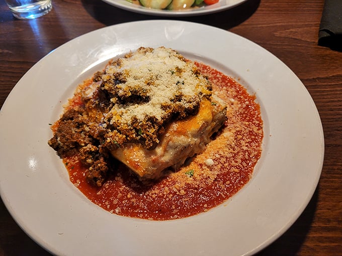 Lasagna that doesn't just sit on the plate—it stands at attention, layers of flavor commanding respect in a pool of vibrant marinara.