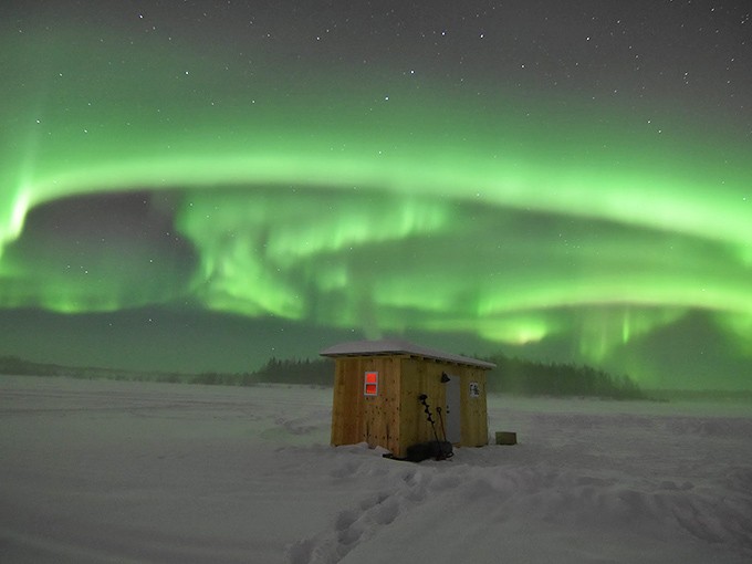 The northern lights dance above a humble ice fishing hut&mdash;nature's most spectacular light show upstaging even North Pole's Christmas decorations.