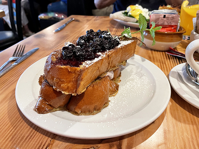 French toast that towers like a delicious skyscraper, crowned with berries that pop against the powdered sugar like edible jewels.