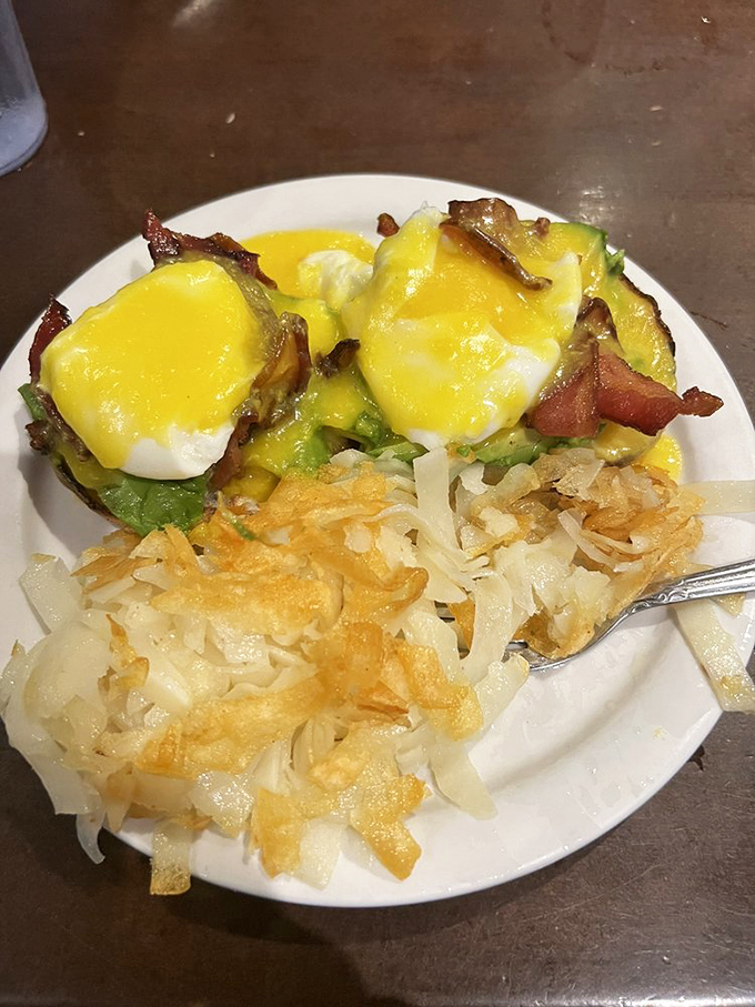 Hollandaise cascades like yellow velvet over this benedict masterpiece. The crispy hash browns stand ready to catch any wayward sauce—nothing goes to waste here.