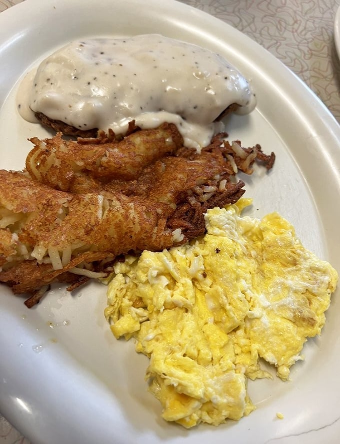 The holy trinity of diner breakfast: fluffy eggs, crispy hash browns, and country gravy cascading over golden-fried deliciousness.