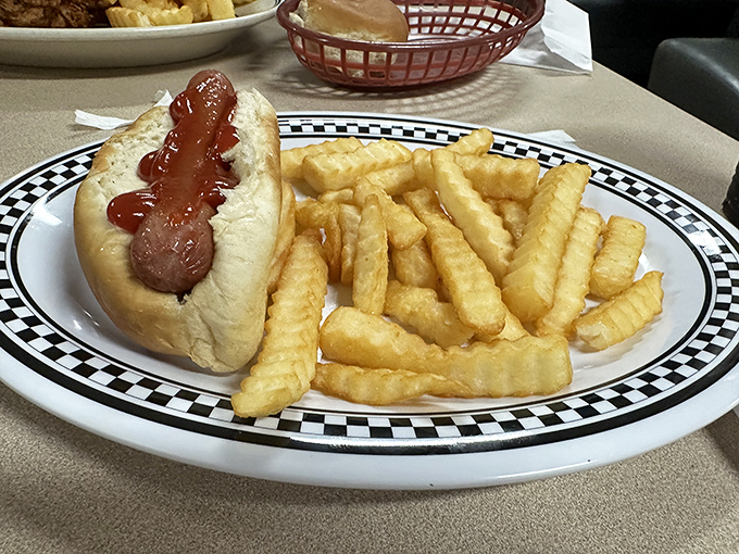 A hot dog and crinkle-cut fries on a checkered-rim plate&mdash;simple pleasures that remind us why some classics never need reinvention.
