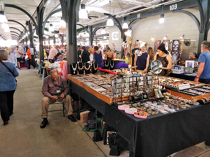 A vendor takes a moment of quiet contemplation amid a dazzling display of jewelry, each piece telling its own New Orleans story.
