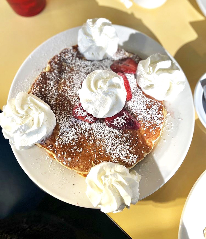 This isn't just a pancake&mdash;it's a fluffy canvas of joy, dusted with powdered sugar and adorned with whipped cream islands in a sea of sweetness.