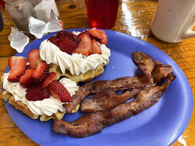 Breakfast perfection: crispy bacon alongside waffles topped with fresh strawberries and whipped cream. The breakfast gods are smiling down on this plate.
