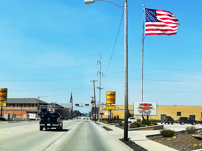 American flag waves proudly over Main Street in small-town Illinois, where local businesses line the quiet road.