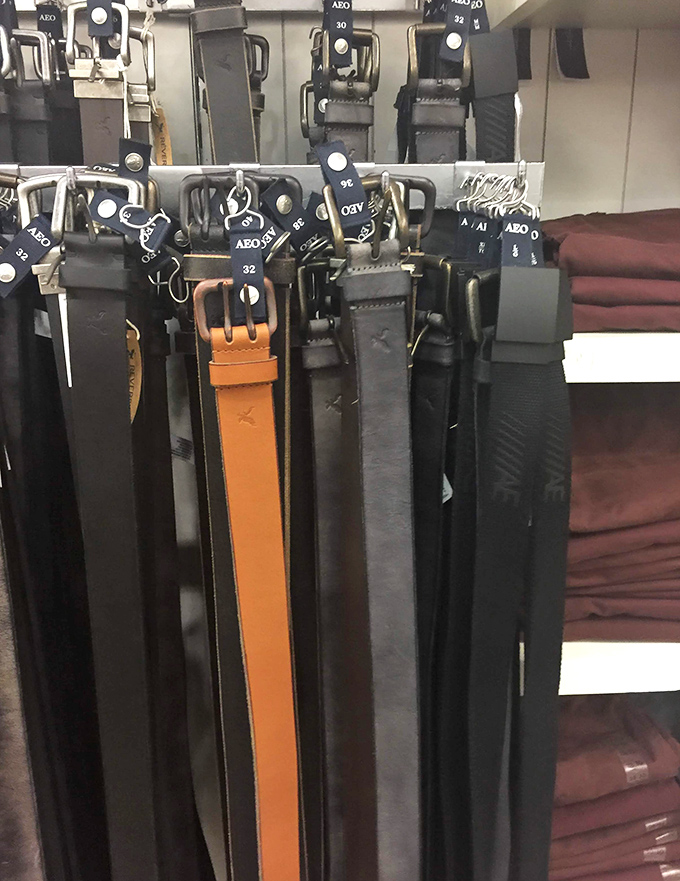 The belt section—where function meets fashion in a symphony of leather. That lone orange standout is the retail equivalent of a rebel yell.