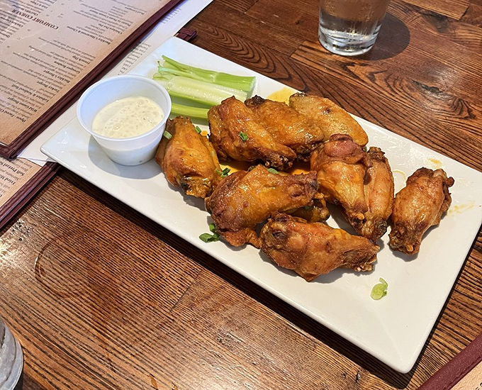These golden chicken wings glisten with promise, accompanied by celery and dipping sauce for the full tavern experience.