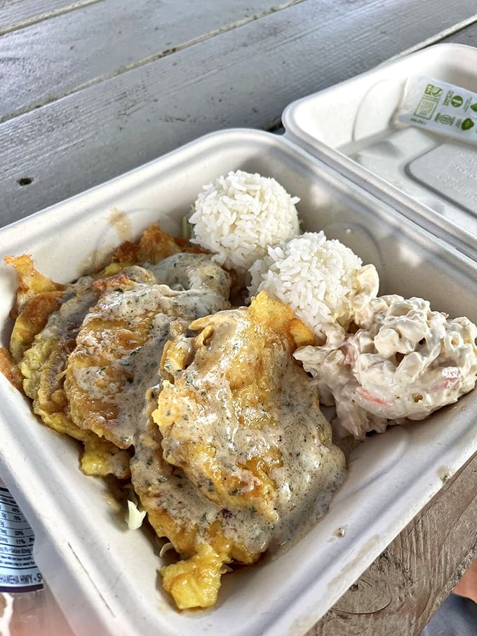 A plate lunch featuring what appears to be eggs smothered in gravy alongside rice and mac salad&mdash;the ultimate surfer's refueling station.