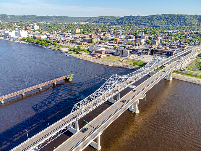 Winona's dramatic landscape showcases the mighty Mississippi River flowing beneath steel bridges, with bluffs standing guard in the distance.