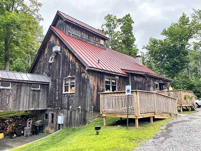 Vermont architecture at its most authentic—weathered barn boards, bright red roof, and a wooden deck that practically begs you to sit with coffee and maple-drenched pancakes.