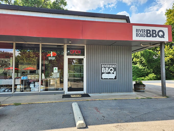 The unassuming red facade of River Road BBQ stands like a beacon of smoky promise against Kentucky's lush greenery.