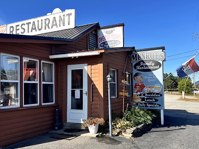 The charming entrance to Munroe's, where hostas frame the doorway and the vintage sign promises breakfast dreams that have kept White Mountain visitors returning for generations.