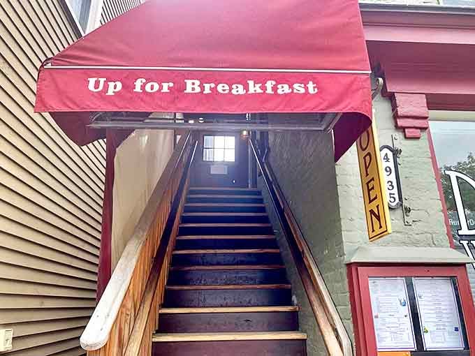 The journey to breakfast nirvana begins with these unassuming stairs, sheltered by a crimson awning that might as well read "Abandon hunger, all ye who enter here."