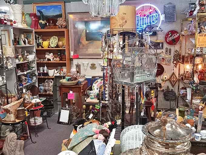 Vintage advertising signs illuminate this packed booth where collectibles, glassware, and decorative items create a mesmerizing treasure hunter's paradise.