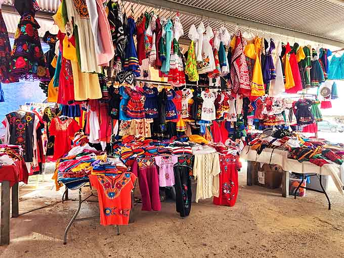 A vibrant explosion of traditional Mexican dresses and colorful clothing transforms this corner of the market into a cultural celebration.