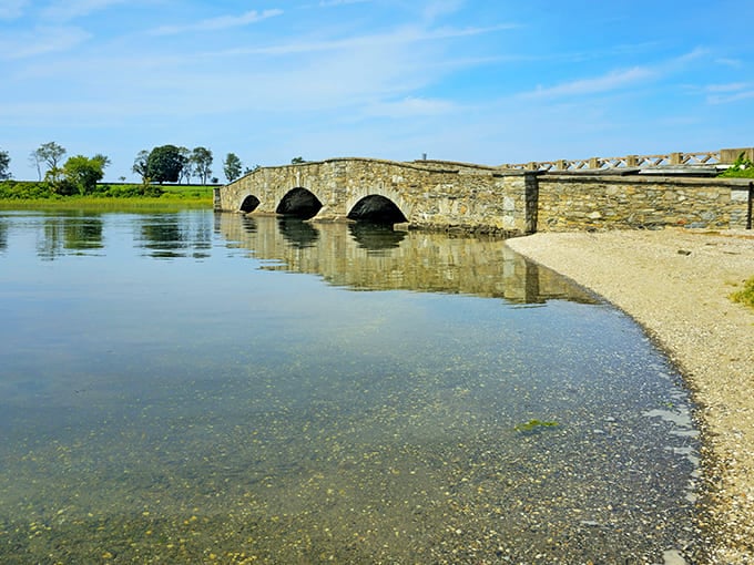 The historic stone bridge at Colt State Park mirrors perfectly in still waters, creating a scene so picturesque it belongs on the Rhode Island state quarter. Nature's own infinity pool with architectural flair.