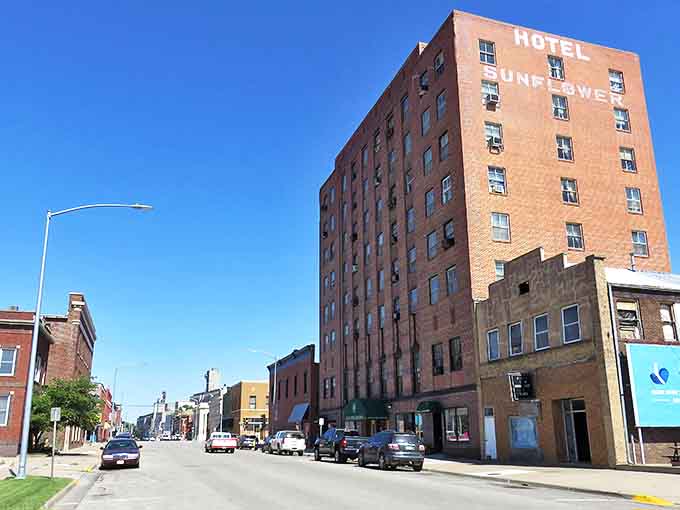 The Hotel Sunflower stands tall against that impossibly blue Kansas sky, a brick sentinel watching over a downtown where rush hour means three cars at a stop sign.