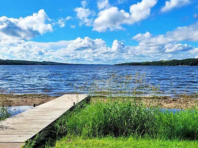 Big Stone Lake stretches toward the horizon like a sapphire highway, with this simple wooden dock serving as your personal launch pad to serenity.