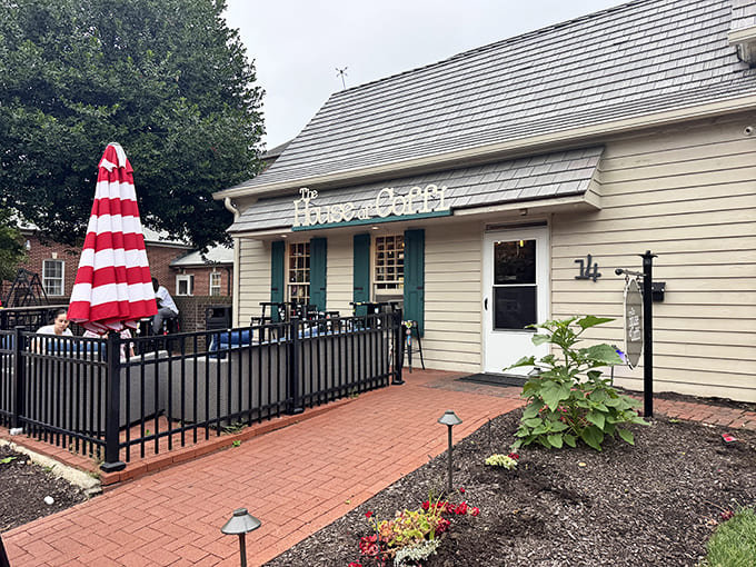 The charming exterior of House of Coffi beckons with its cream siding, brick pathway, and that iconic red-striped umbrella&mdash;like a coffee oasis in downtown Dover.