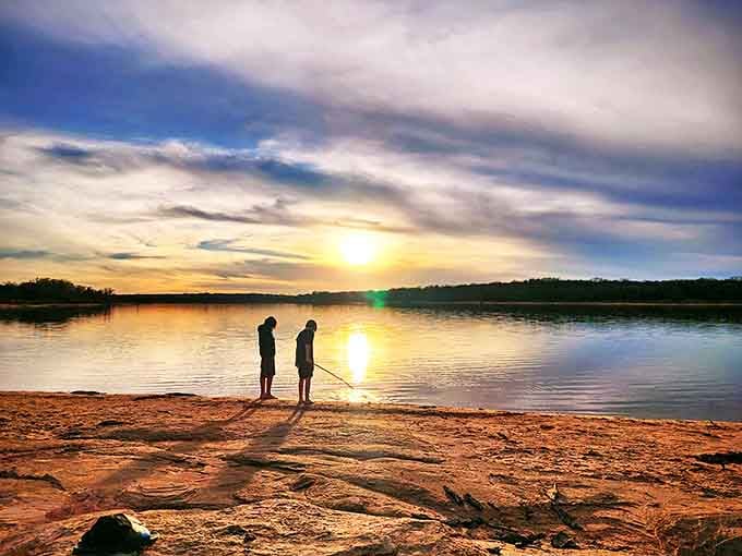Two silhouettes against a sunset that looks like it was ordered from a premium catalog. Lake Thunderbird's daily light show requires no tickets, just perfect timing.