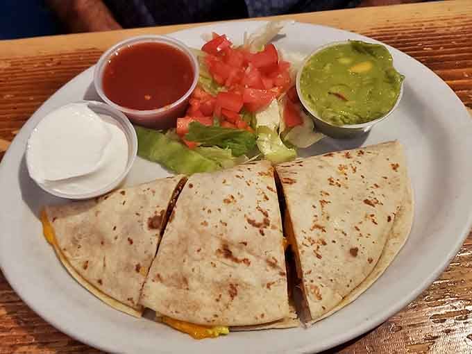 A quesadilla that understands the assignment: melty cheese, fresh toppings, and those little cups of salsa and guacamole for perfect customization.