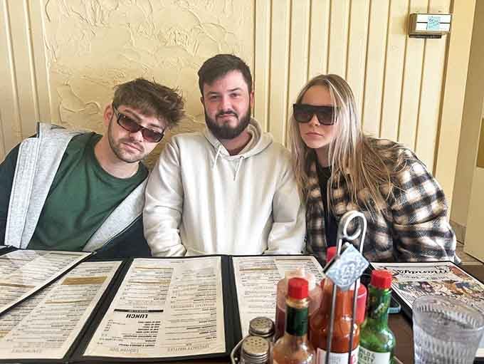 Three diners contemplate life's greatest question: what to order when everything sounds amazing. The condiment caddy stands ready for whatever decision they make.