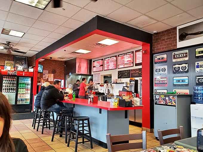 Command central for burger magic. The bright red counter frames the kitchen where ordinary ingredients transform into extraordinary meals while vintage cassette art nods to simpler times.