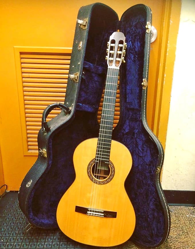 A classical guitar nestled in its blue velvet case&mdash;someone's musical journey paused, now waiting for your fingers to continue the melody.