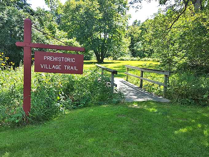 The Prehistoric Village Trail beckons with a rustic bridge that seems to transport visitors not just across water, but across time.