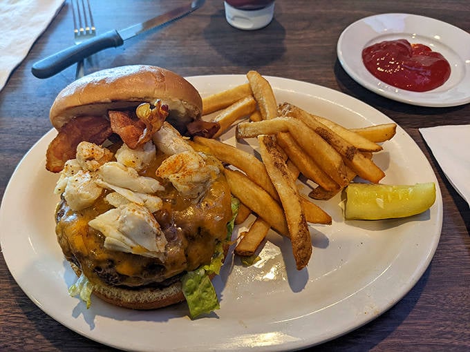 The holy trinity of comfort food: a perfectly charred burger crowned with jumbo lump crab, golden fries, and that essential pickle slice standing guard.