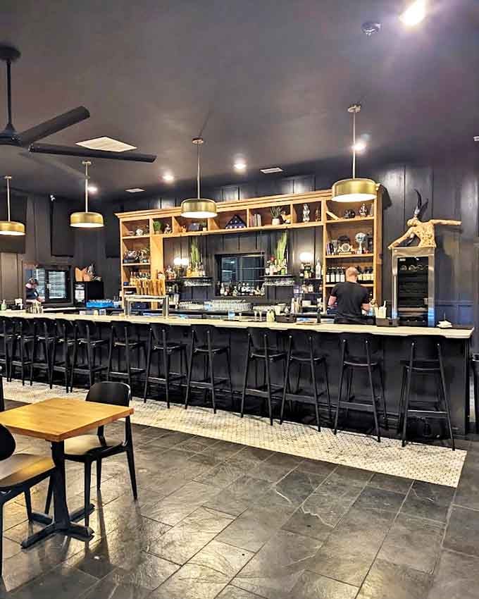 Pendant lights cast a golden glow over the stylish bar area, where black stools invite patrons to pull up and stay awhile.