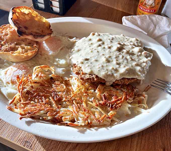 Country gravy cascading over crispy chicken like a delicious waterfall. Those hash browns aren't a side dish—they're an essential supporting character.