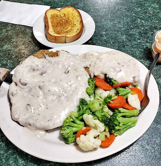 Chicken fried steak hidden beneath a blanket of peppery gravy, with a side of vibrant vegetables playing the role of your conscience.