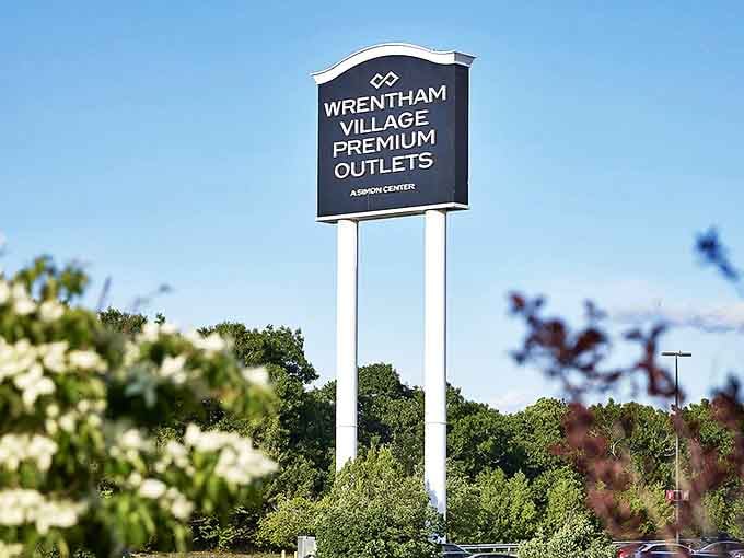 The iconic Wrentham Village sign stands tall against blue skies, like a retail lighthouse guiding bargain hunters safely to discount shores.