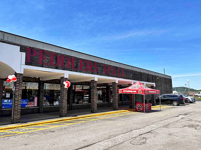 Red letters against blue sky&mdash;the Peddlers Mall entrance promises adventure within those brick columns, where everyday treasures await discovery just beyond those glass doors.